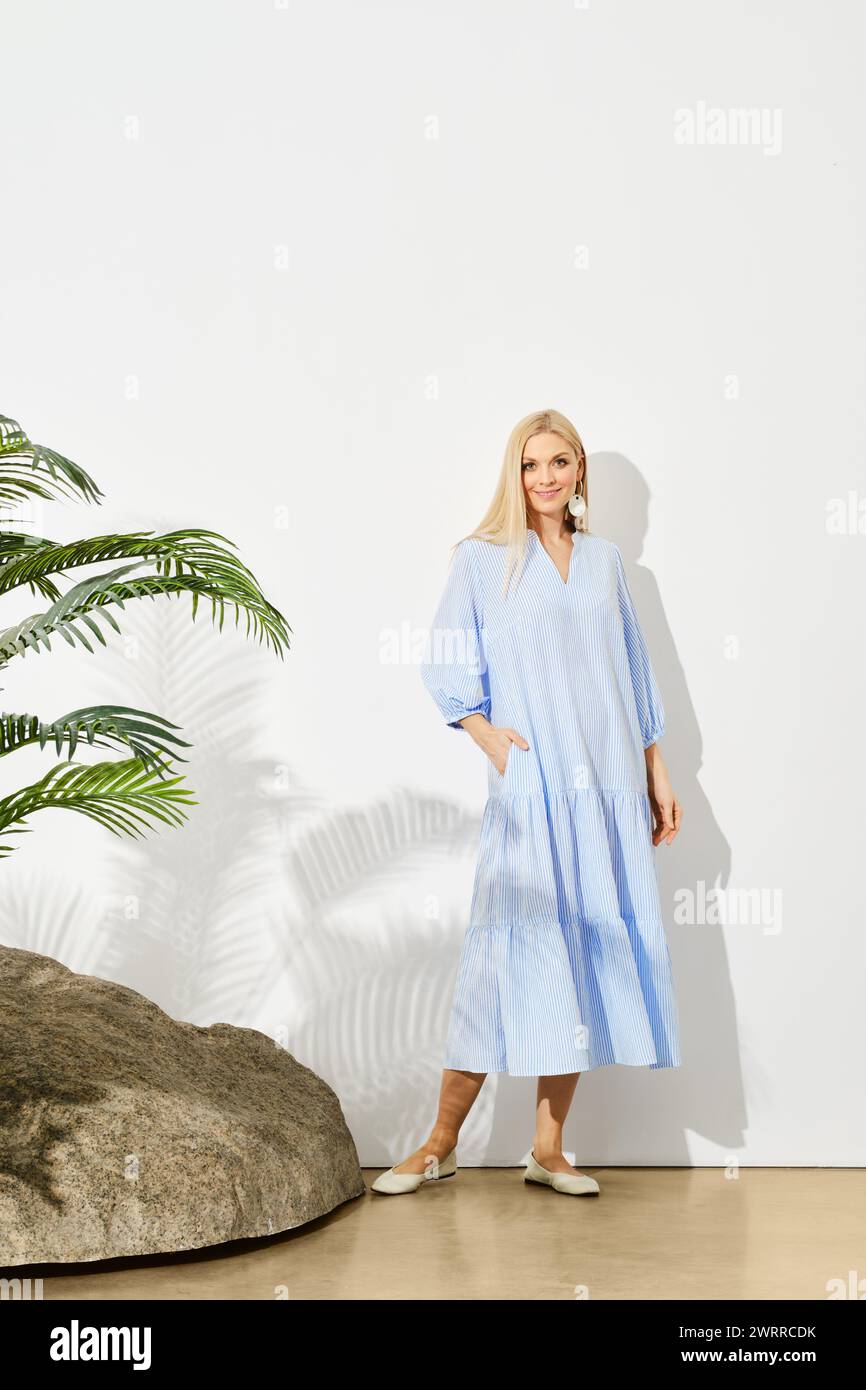 Pretty woman demonstrates long loose blue loose dress, standing next to ...