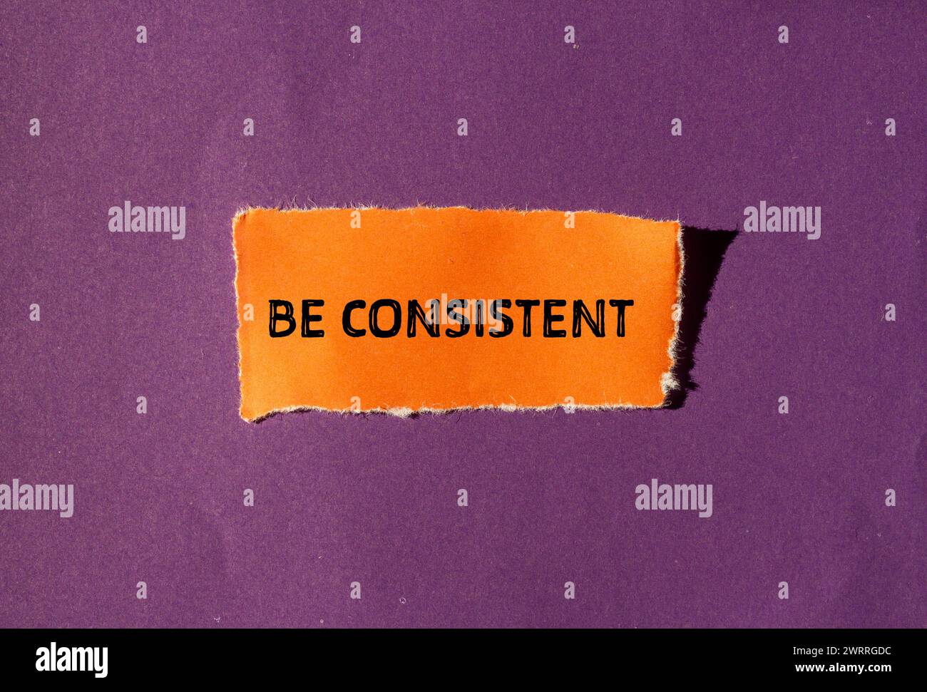 Be consistent words written on orange torn paper with purple background ...