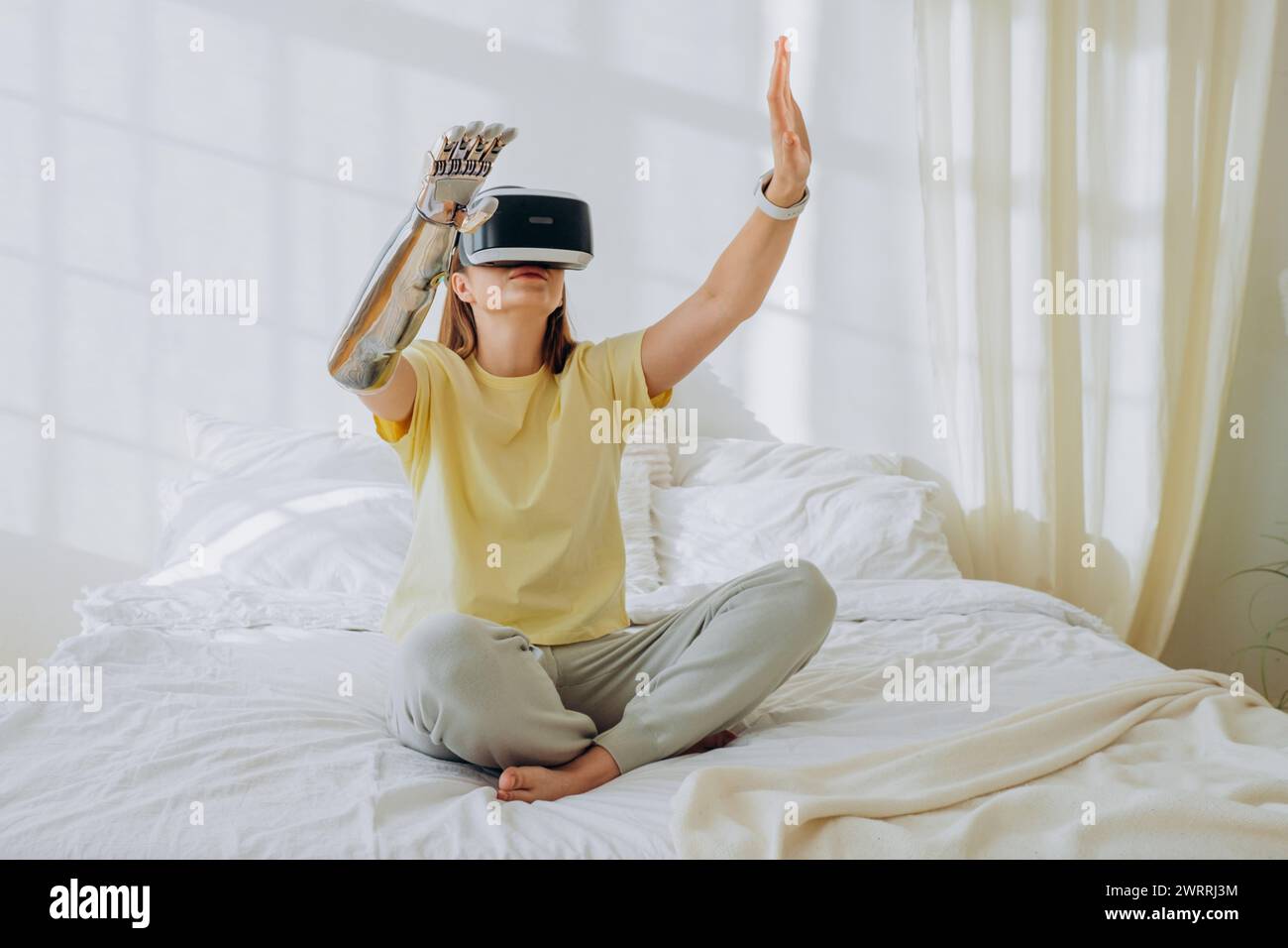 Seated comfortably on her bed, a young woman with a robotic arm ...