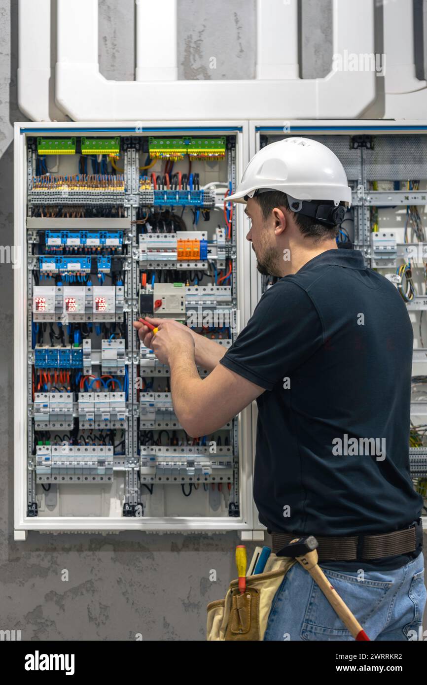 A male electrician works in a switchboard using an electrical ...