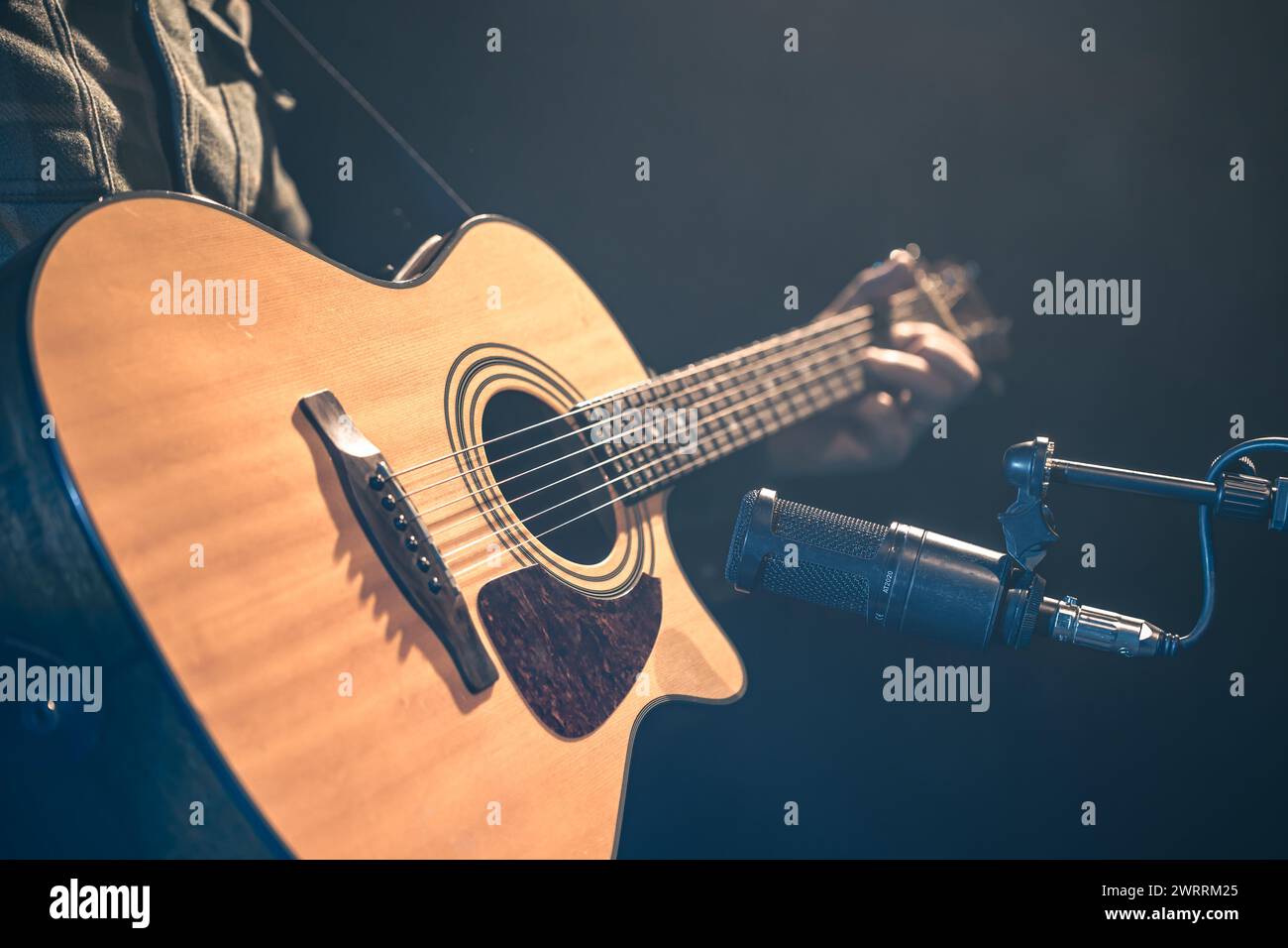 Male musician playing acoustic guitar behind microphone in recording ...