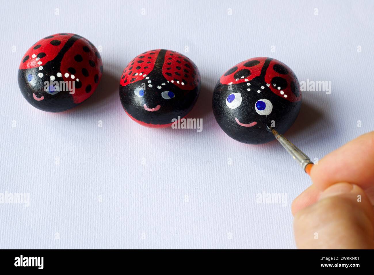 hand painting three stones as cute ladybugs on white paper background ...