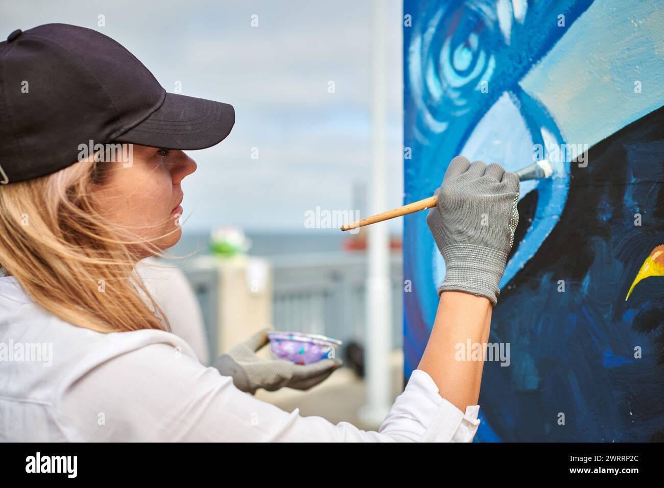 Female painter in black cap draws picture with paintbrush on canvas for ...