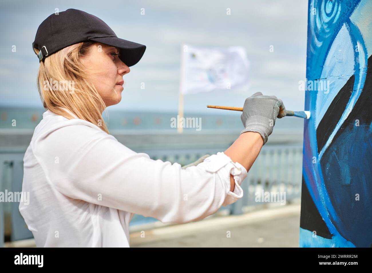 Female painter in black cap draws picture with paintbrush on canvas for ...