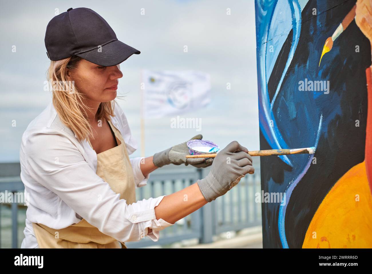 Female painter in black cap draws picture with paintbrush on canvas for ...