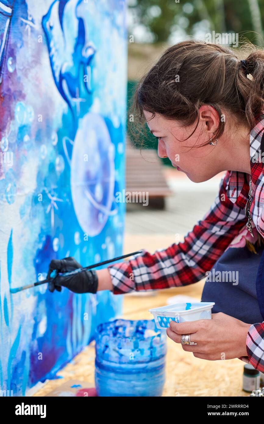 Female painter draws picture with paintbrush on canvas for outdoor ...