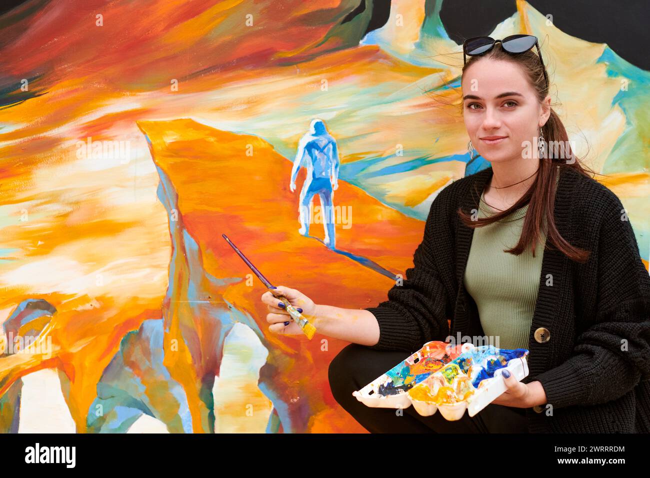Happy female painter holding palette and brush against backdrop of her ...