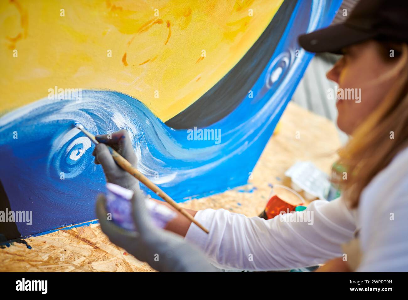 Female painter in black cap draws picture with paintbrush on canvas for ...