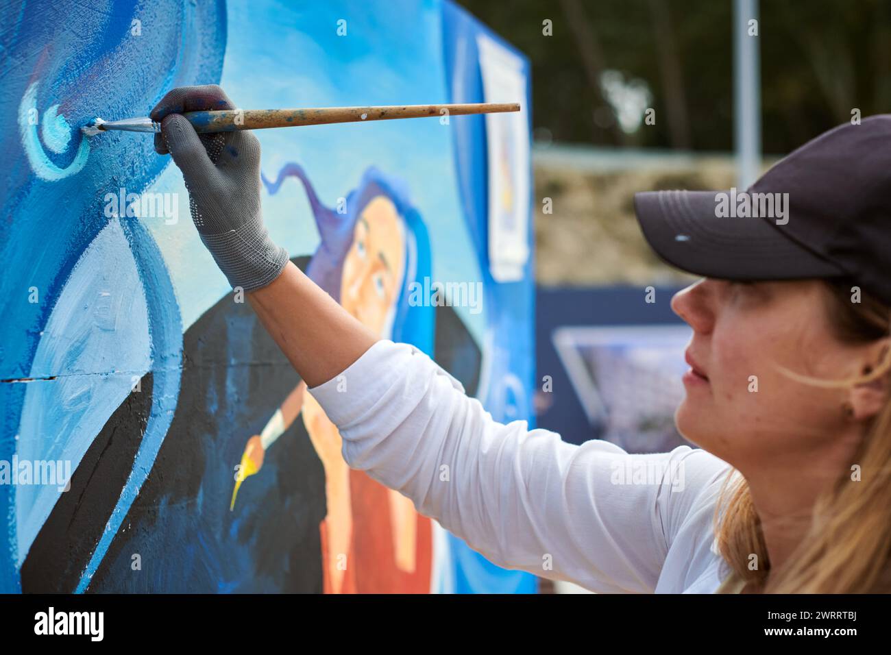 Female painter in black cap draws picture with paintbrush on canvas for ...