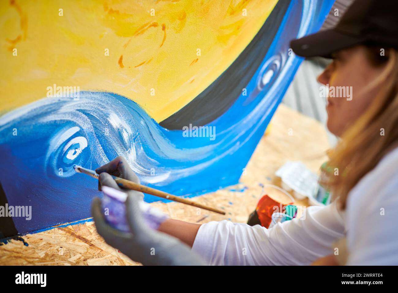 Female painter in black cap draws picture with paintbrush on canvas for ...