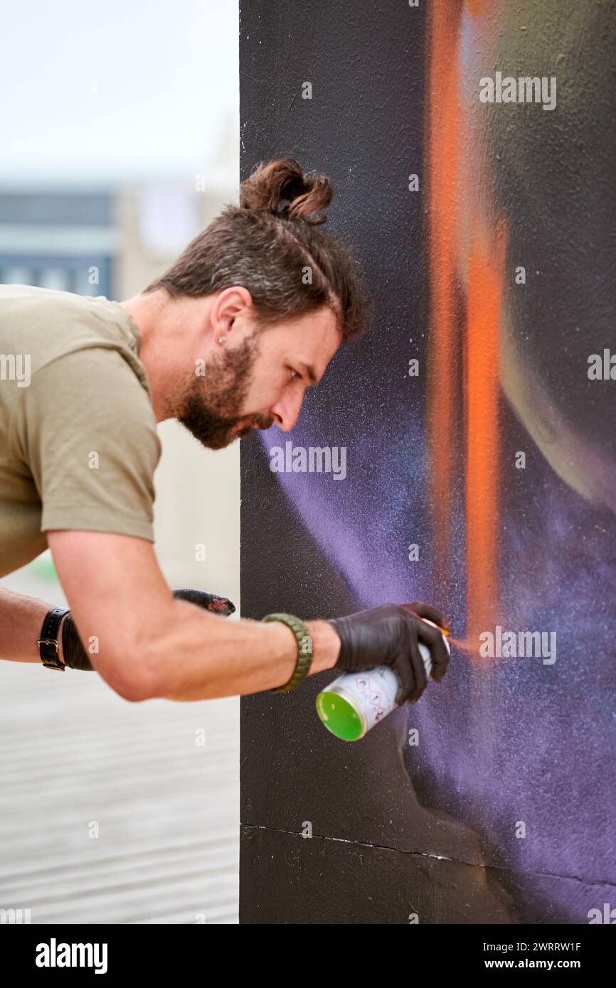 Attractive male artist is painting picture with paint spray can ...