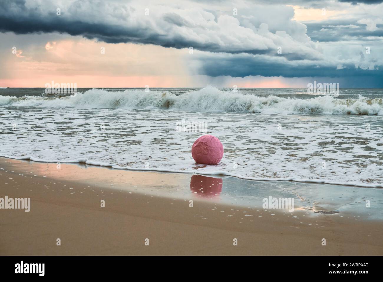 Large pink sphere lapped by waves against seashore against horizon and ...