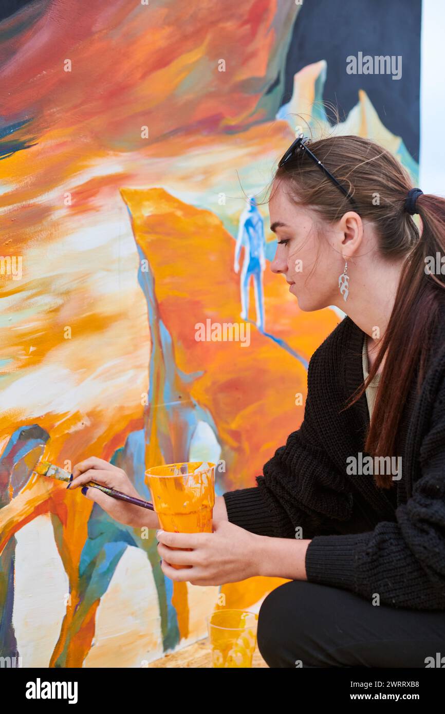 Attractive female painter passionately draws picture with paintbrush ...