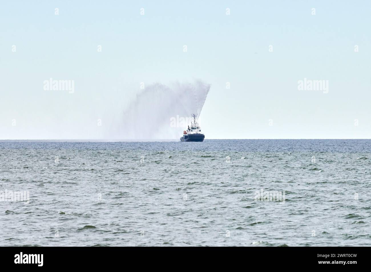 Fireboat ship sails on open sea directing jets of water to sides ...