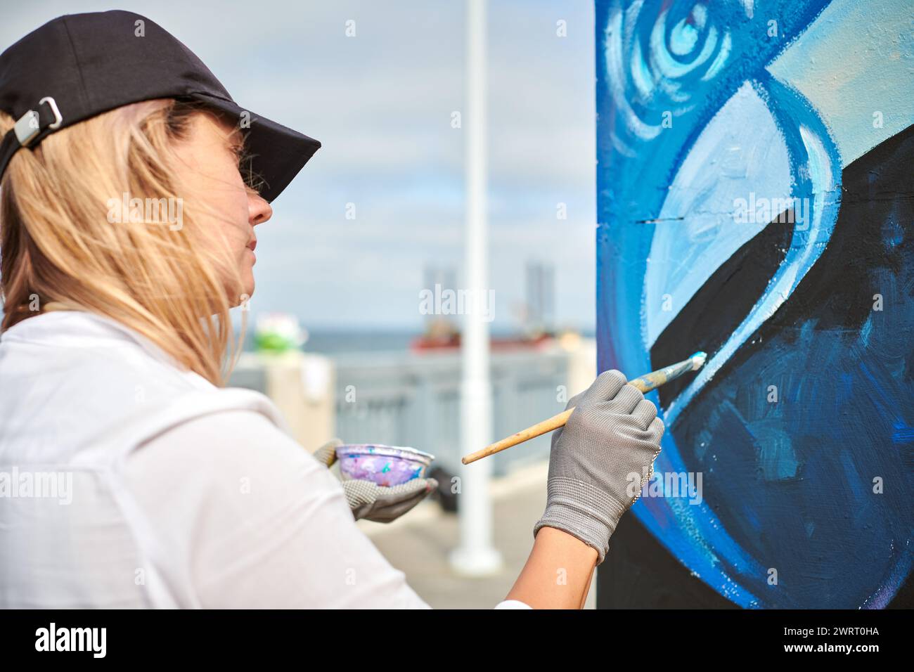 Female painter in black cap draws picture with paintbrush on canvas for ...