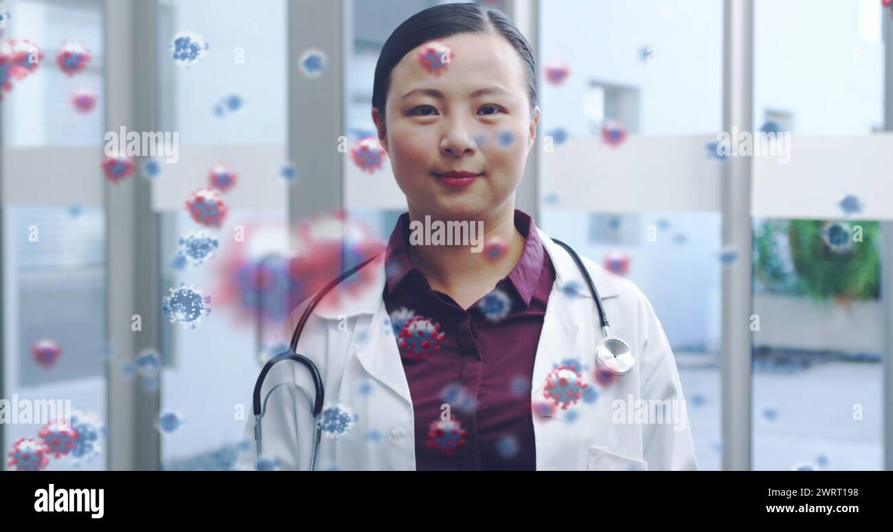 Asian female doctor smiles behind a digital composite of Covid-19 cells ...