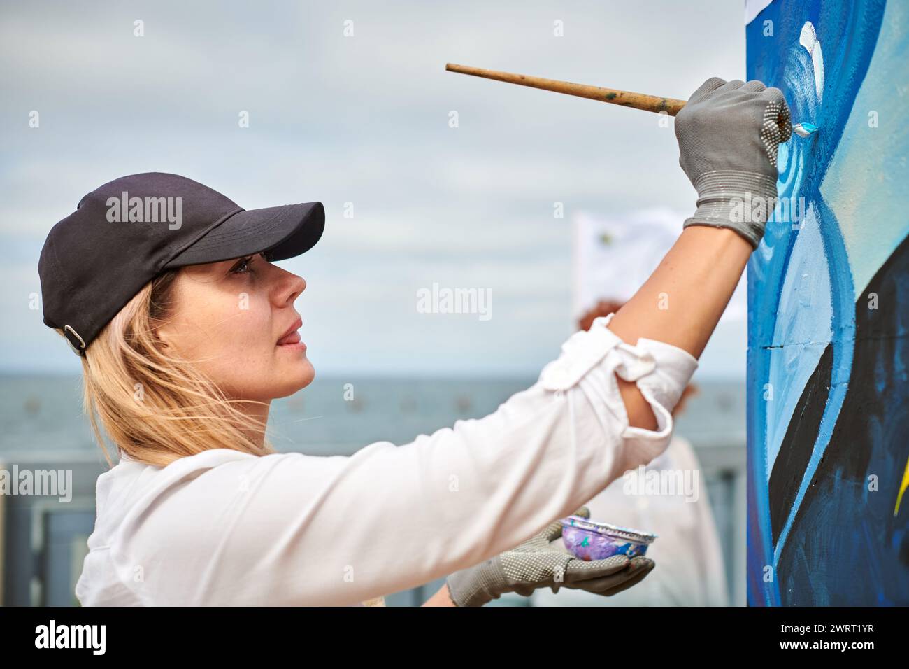 Female painter in black cap draws picture with paintbrush on canvas for ...