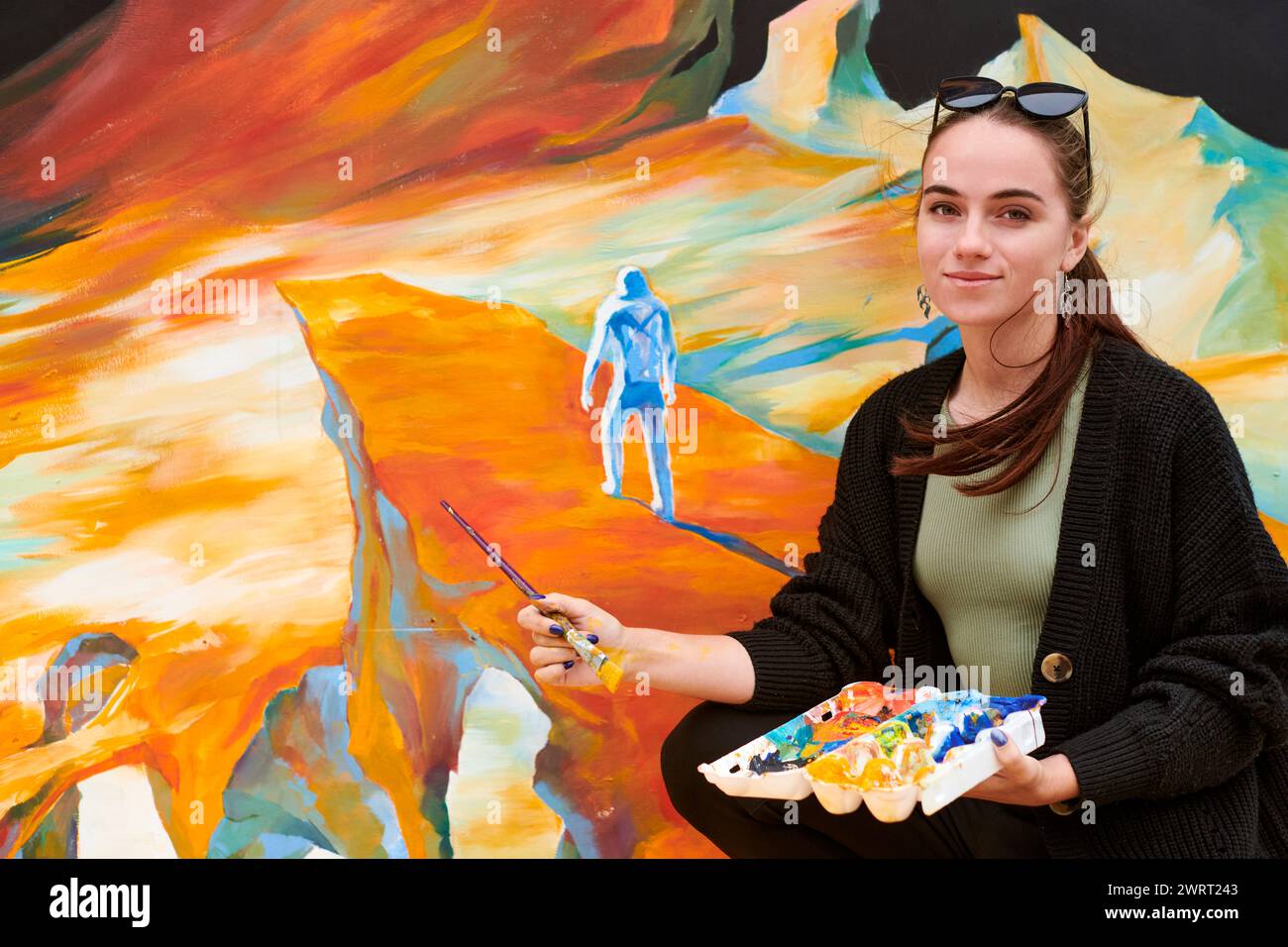 Happy female painter holding palette and brush against backdrop of her ...