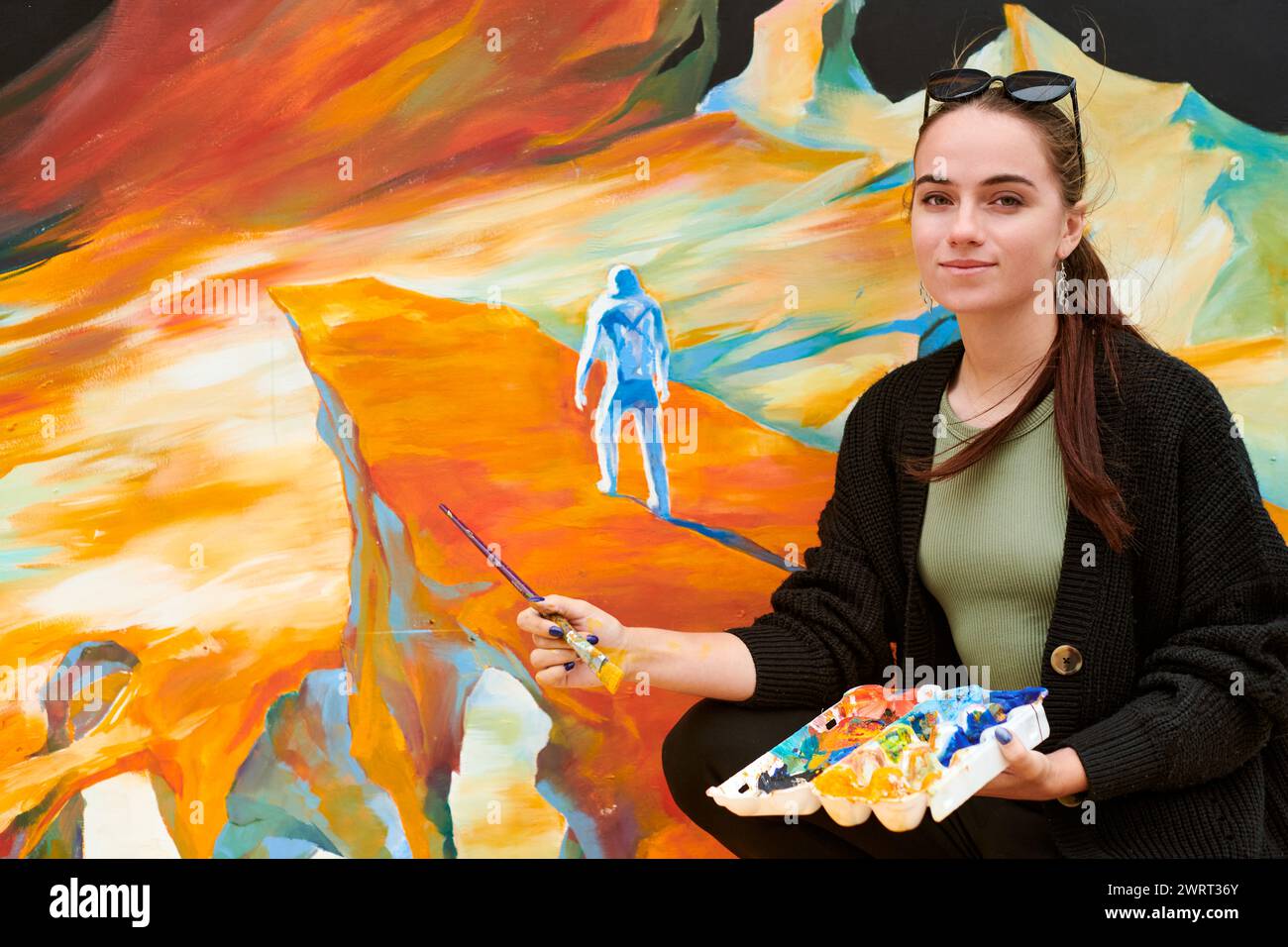 Happy female painter holding palette and brush against backdrop of her ...