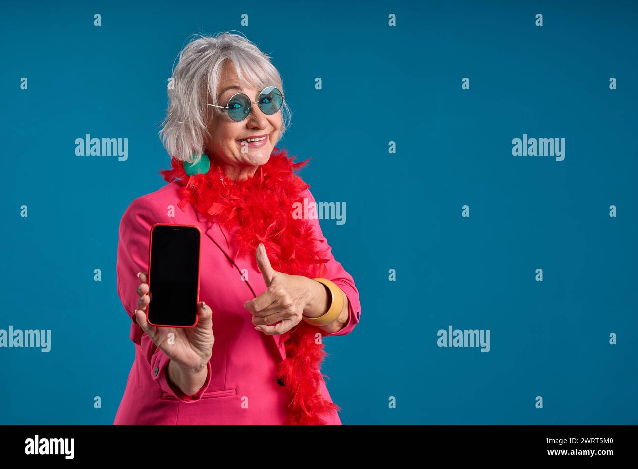 Tech-savvy senior showcasing smartphone and doing thumbs up Stock Photo ...