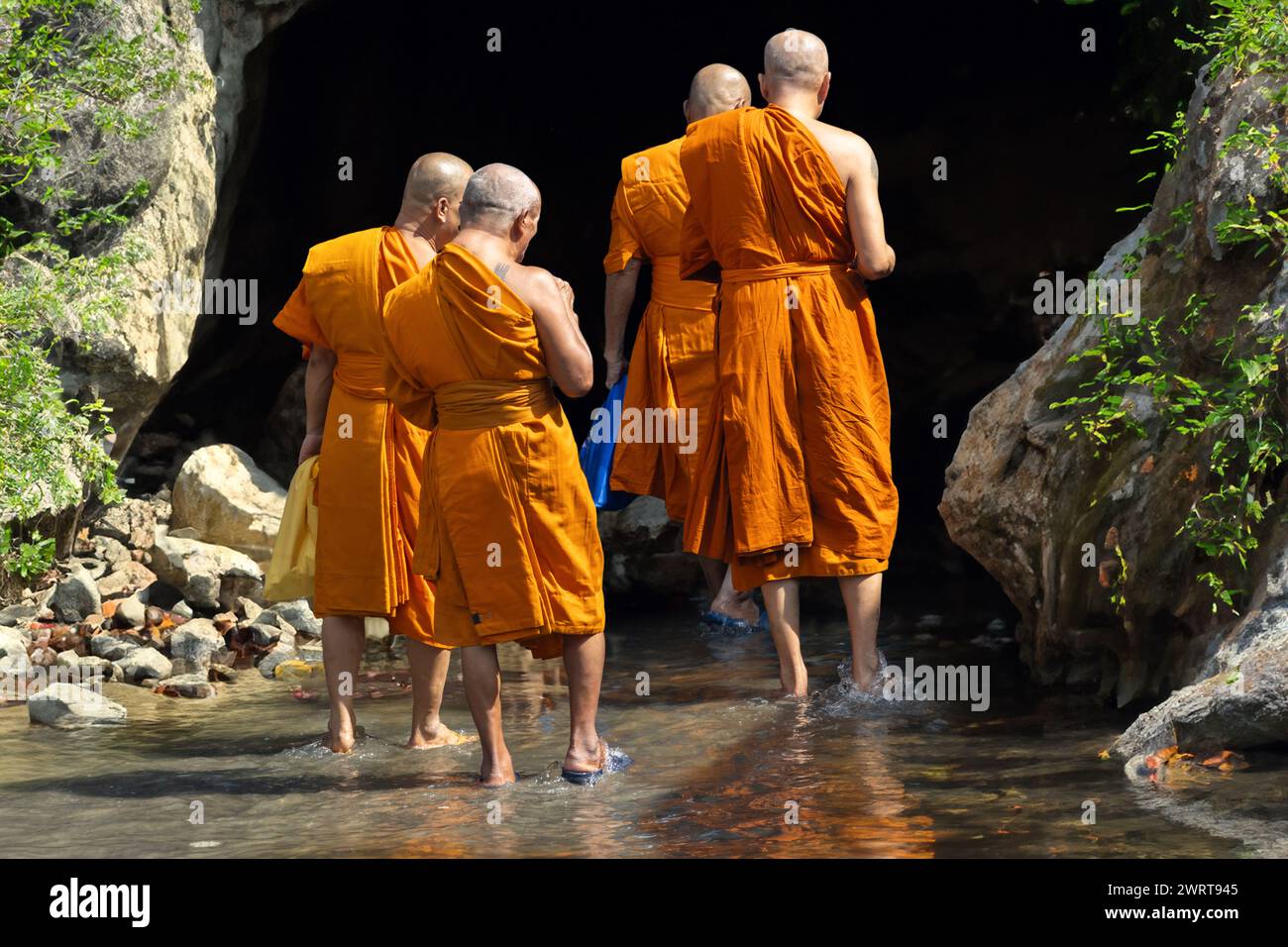 A group of monks walk through a stream to a cave Stock Photo - Alamy