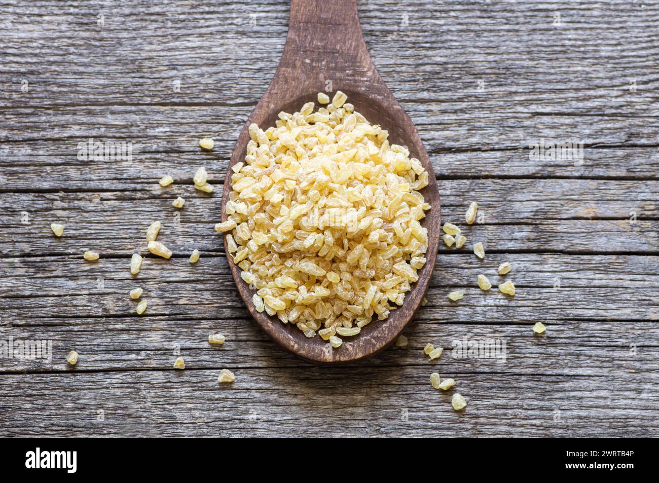 Dry bulgur wheat grains in bowl or spoon on table. Heap of uncooked ...