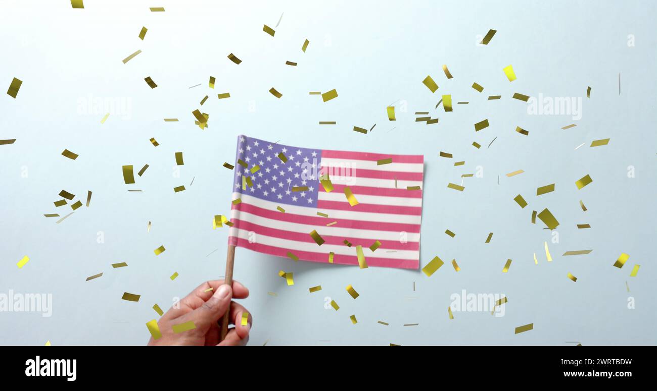 Image of confetti falling over hand holding flag of united states of ...