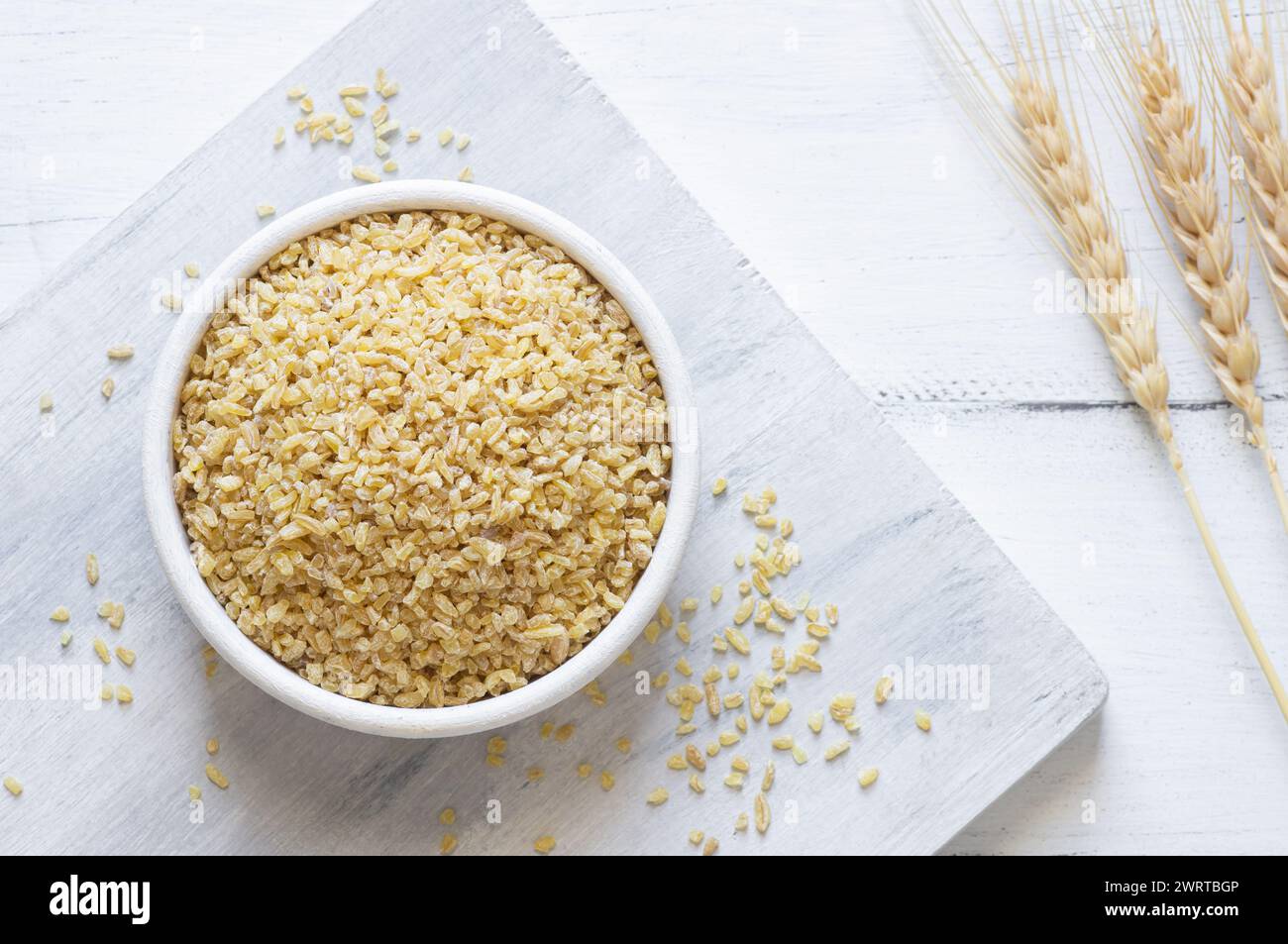 Dry bulgur wheat grains in bowl or spoon on table. Heap of uncooked ...