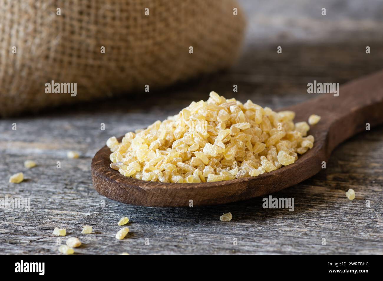Dry bulgur wheat grains in bowl or spoon on table. Heap of uncooked ...