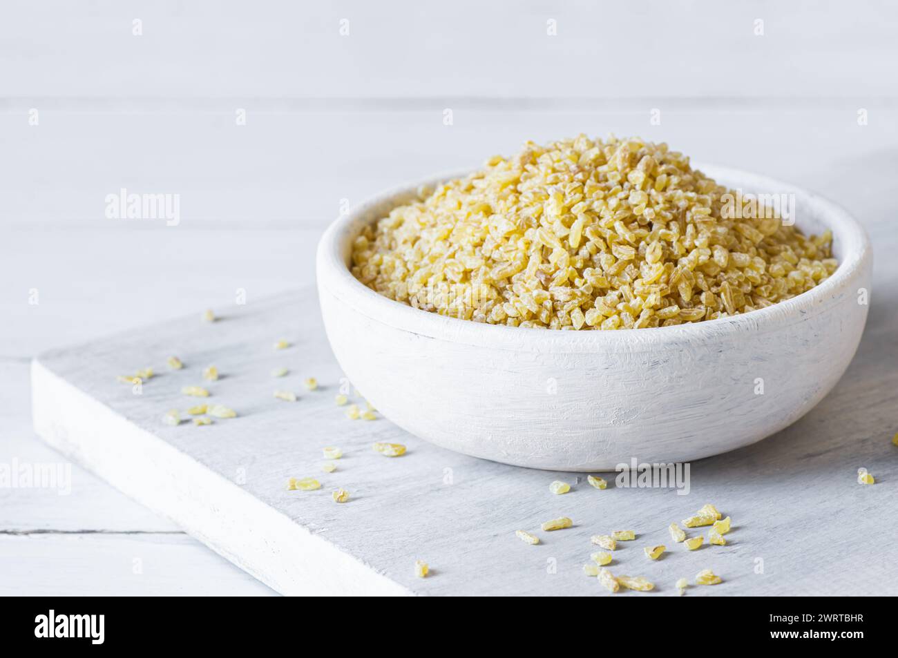 Dry bulgur wheat grains in bowl or spoon on table. Heap of uncooked ...