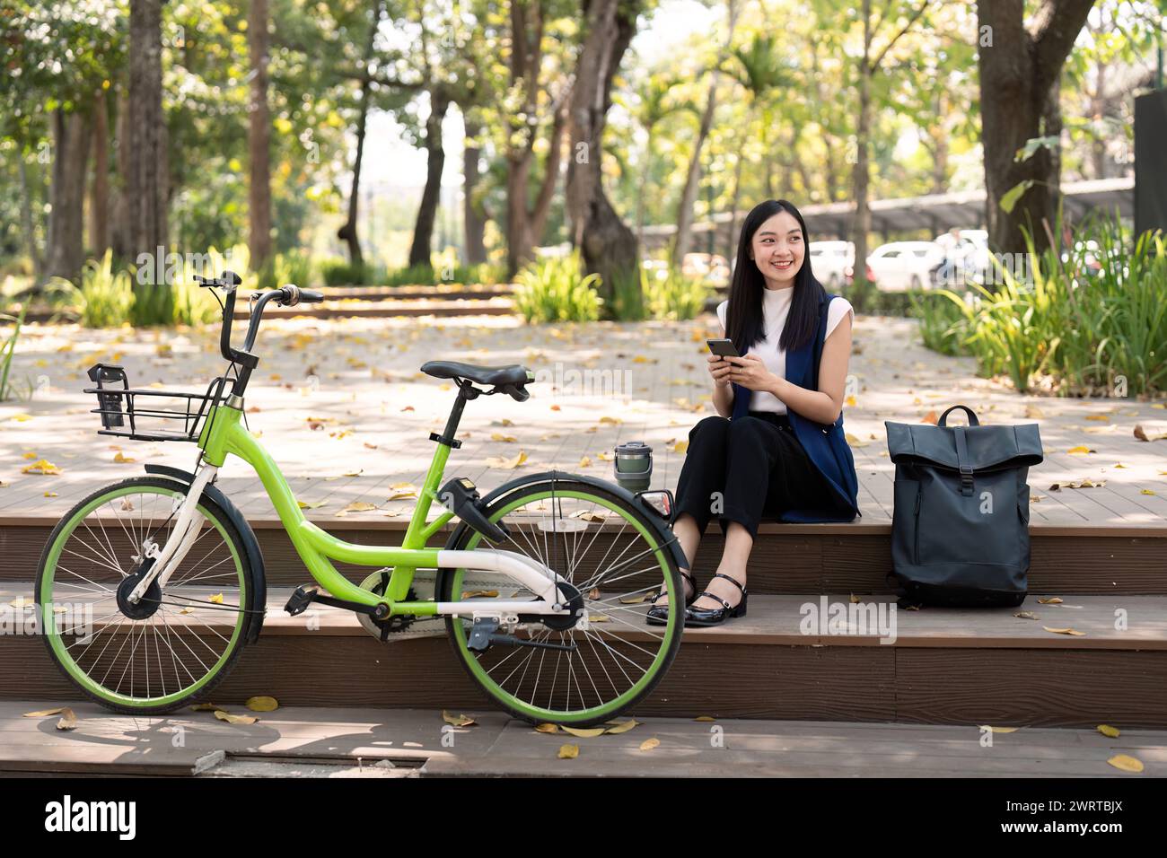 Asian businesswoman with bicycle using smartphone and sitting outside ...