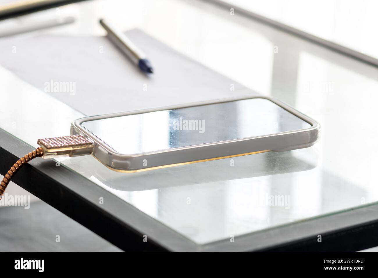 A mobile phone with an attached cable is lying on the glass table top ...