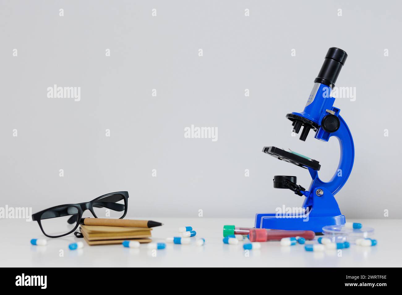 Blue microscope, eyeglasses and pills on white table Stock Photo - Alamy