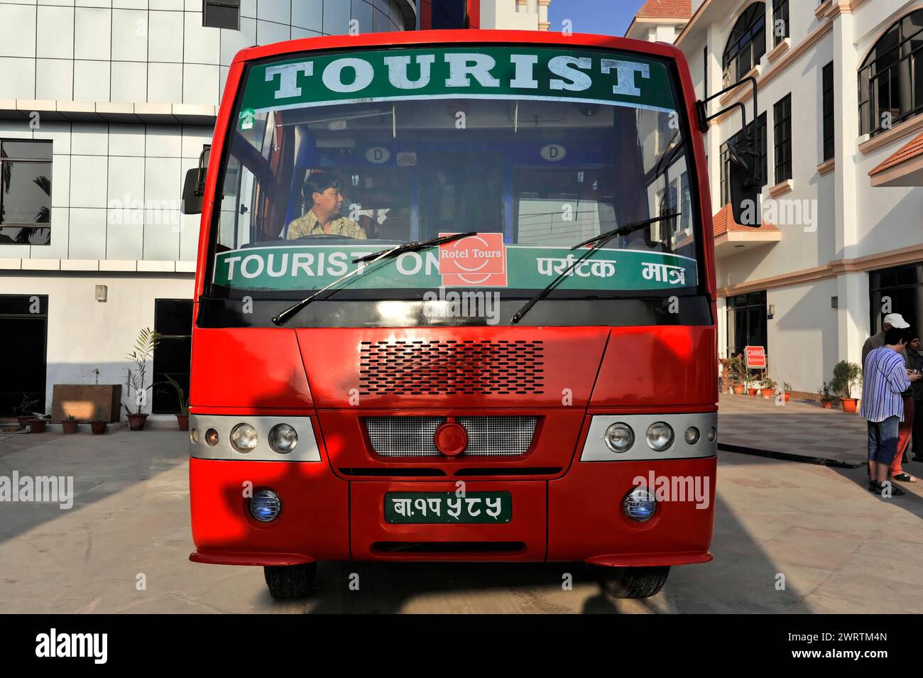 A red tourist bus stands in front of a light-coloured building ...