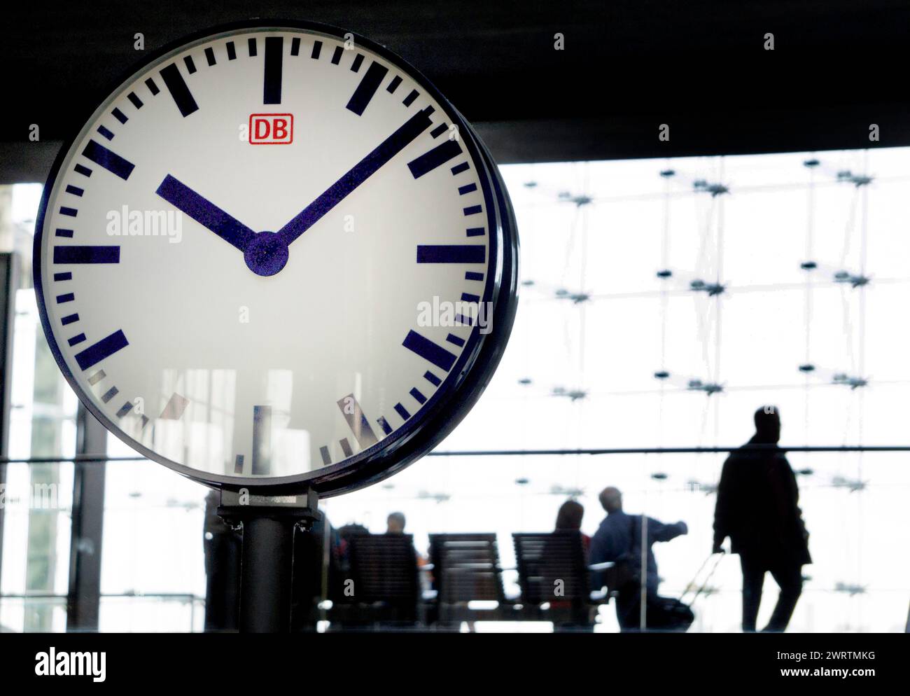 Large station clock, Deutsche Bahn passengers sitting on a bench at ...