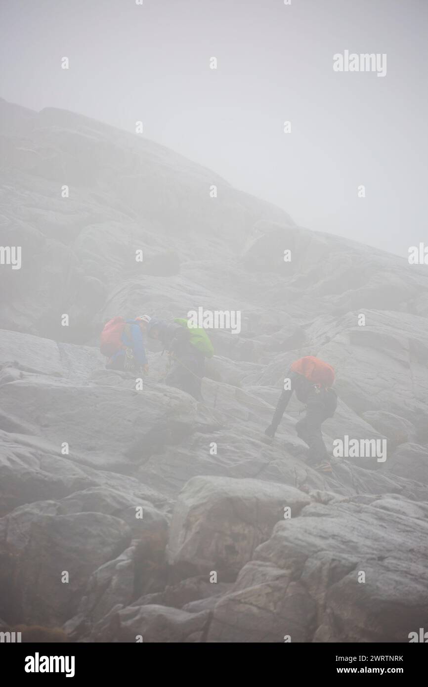 Rear view of distant rock climbers scaling a mountain rock face in the ...