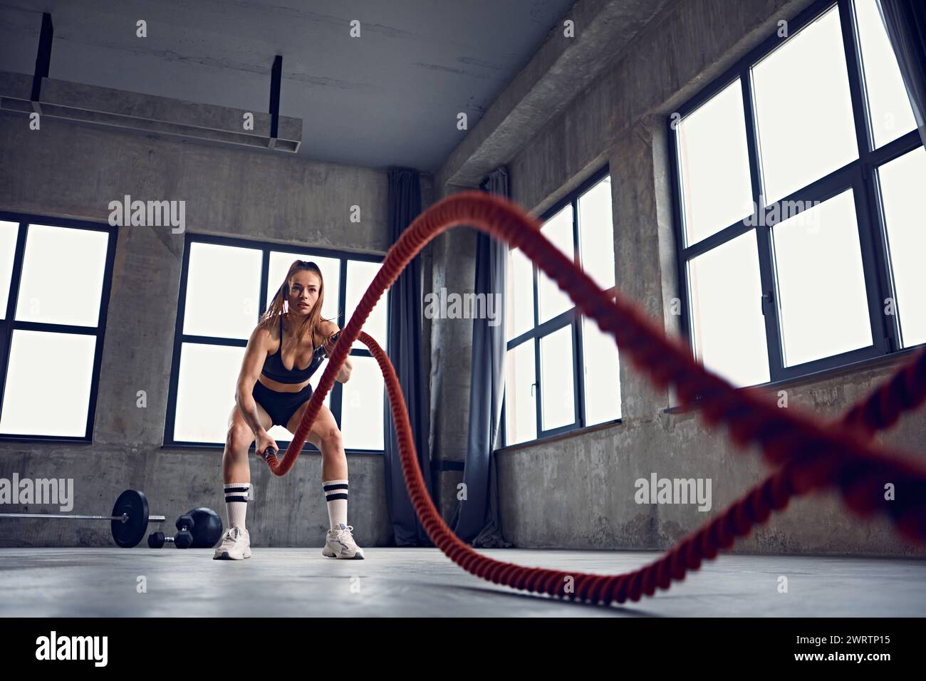 Dynamic portrait of active, athletic woman using battle rope for ...