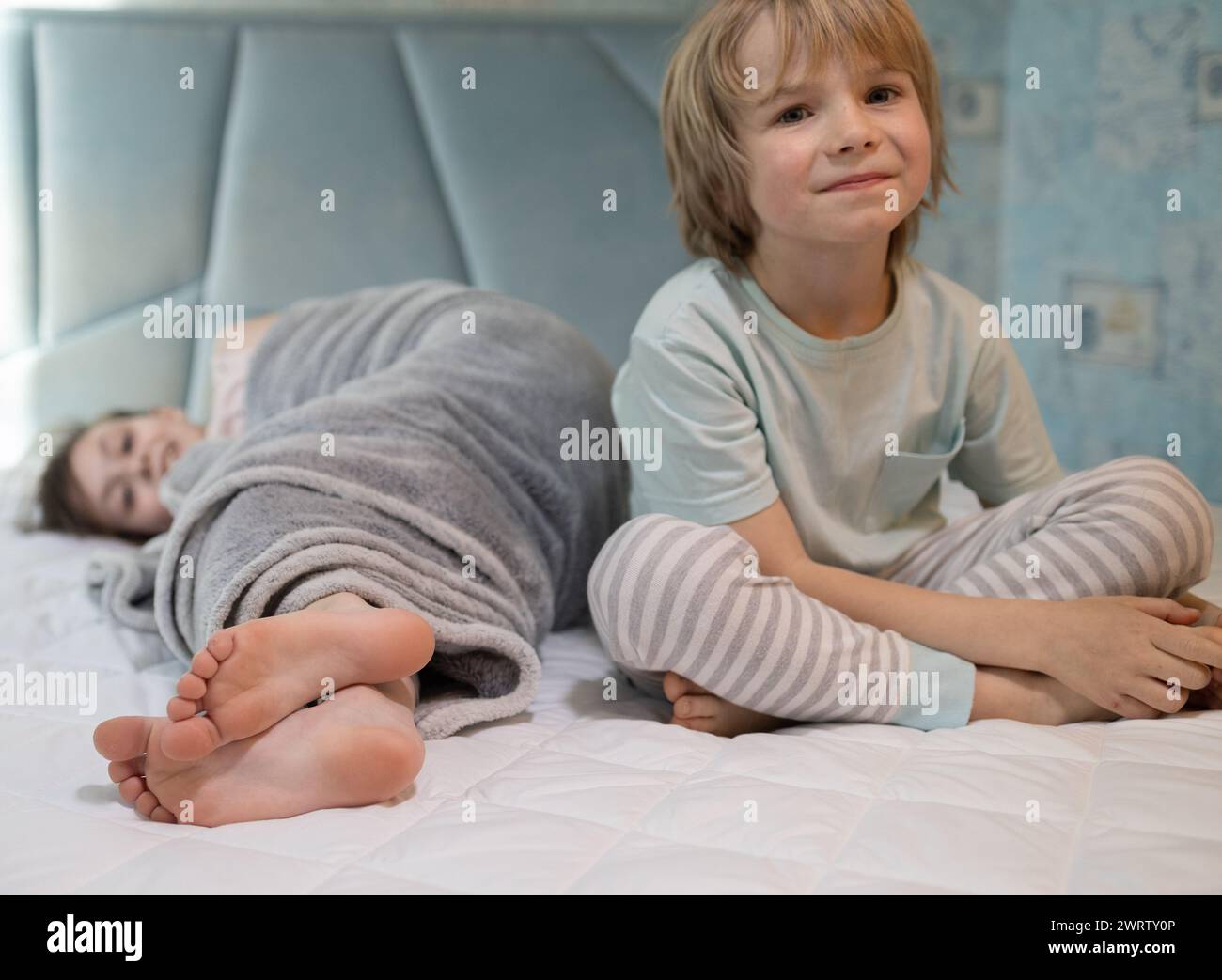 Two barefoot children in pajamas, brother and sister, play on bed at ...