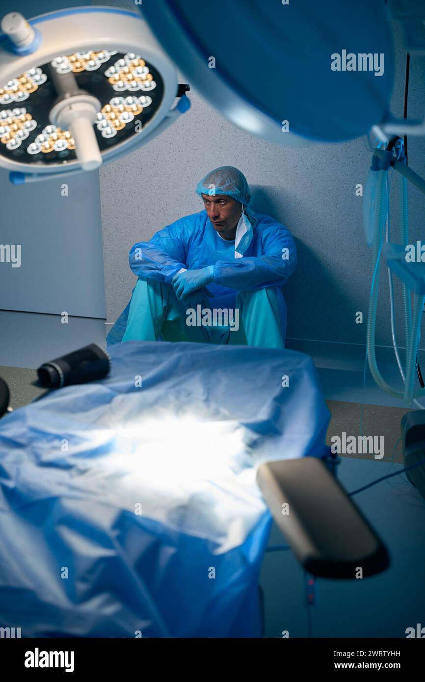 Tensed surgeon man sitting on floor in operating room Stock Photo - Alamy