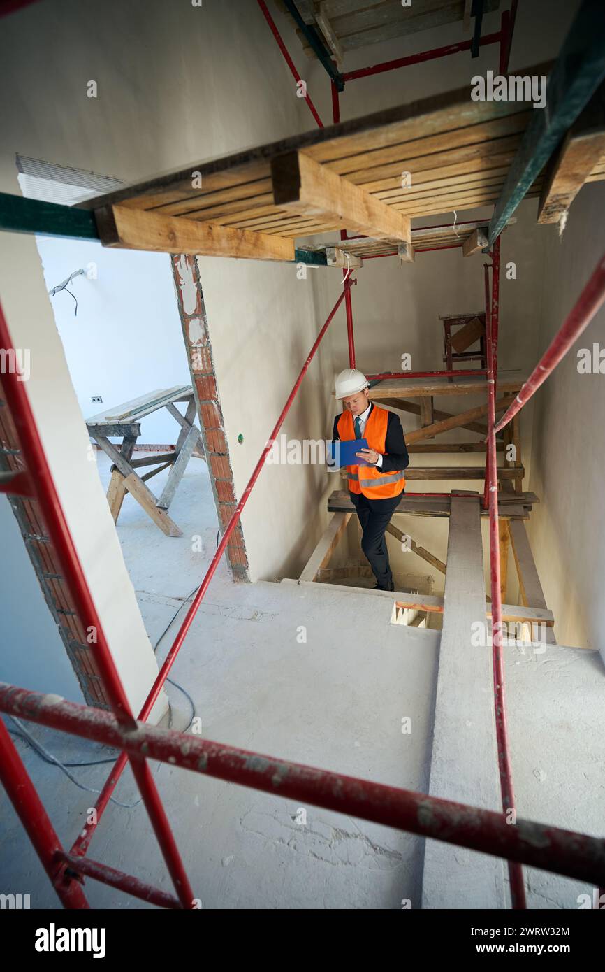 Thoughtful male construction manager walks up stairs in house while ...