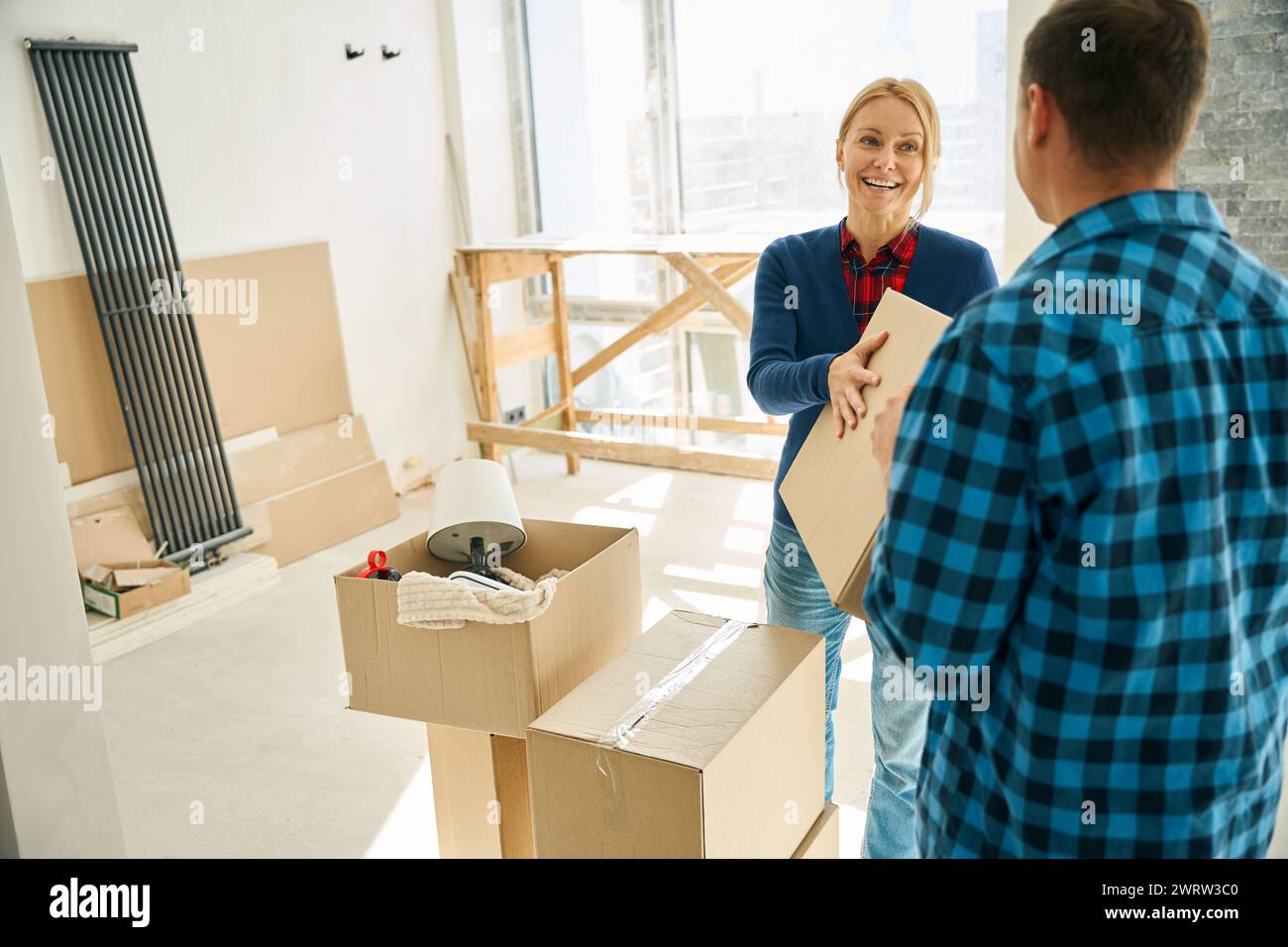 Cheerful lady giving box to man who standing near her and helping to ...