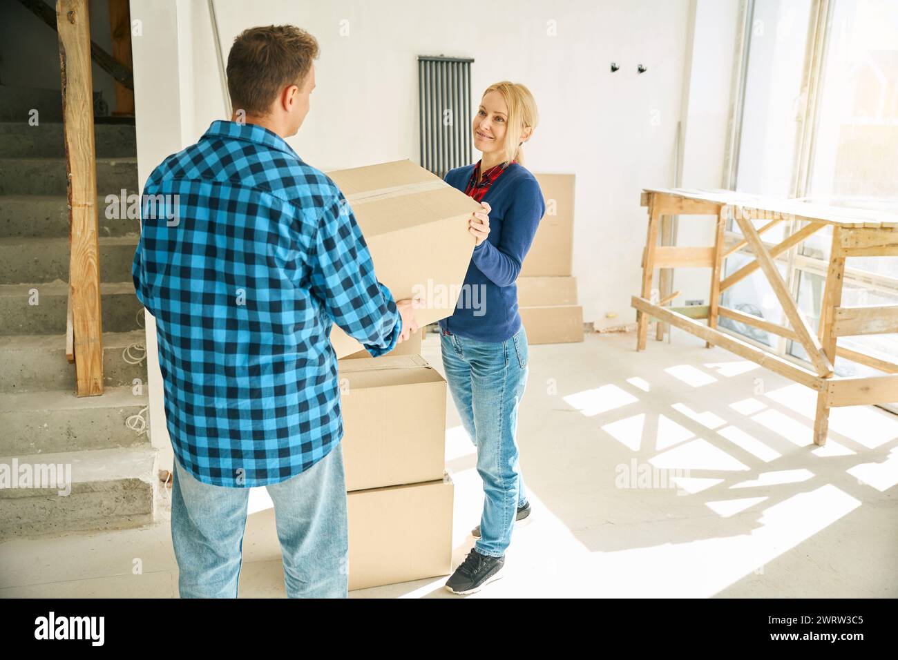 Happy adult couple standing in room and putting cardboard boxes in ...