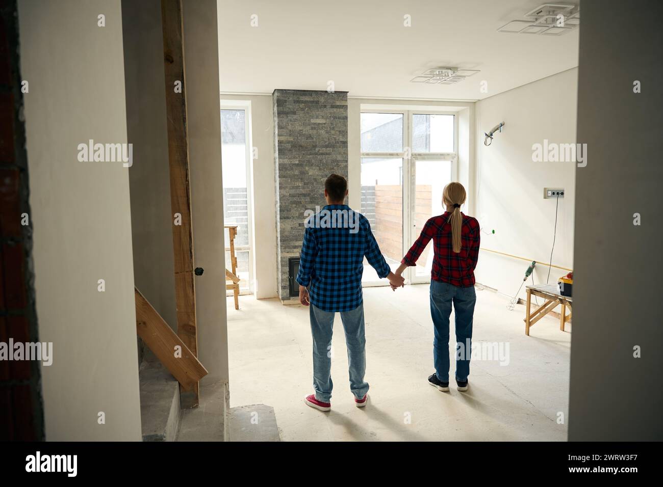Back view picture of lady and man standing in uncompleted room while ...