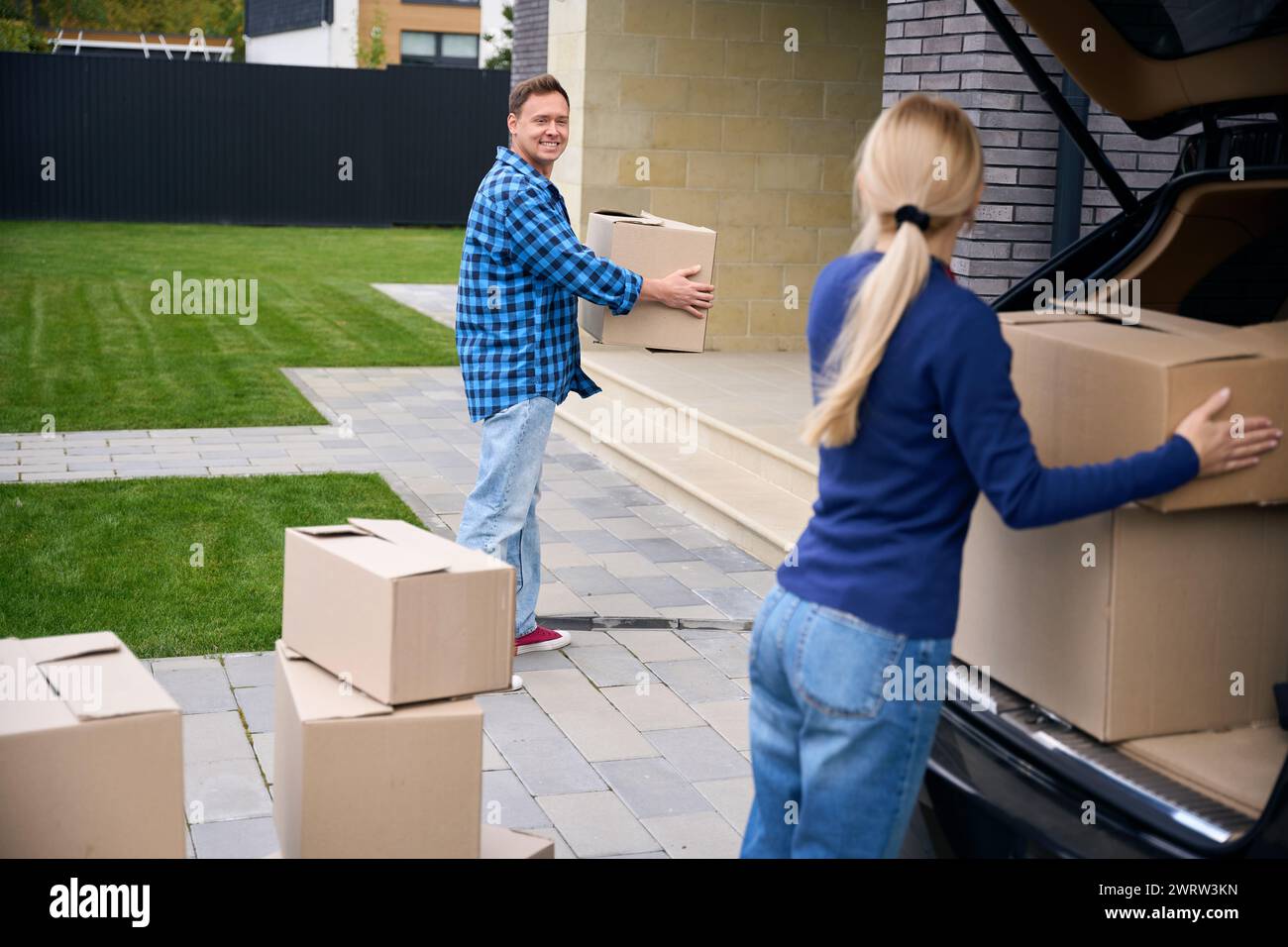 Lady standing and unloading cardboard box out of car trunk while joyful ...