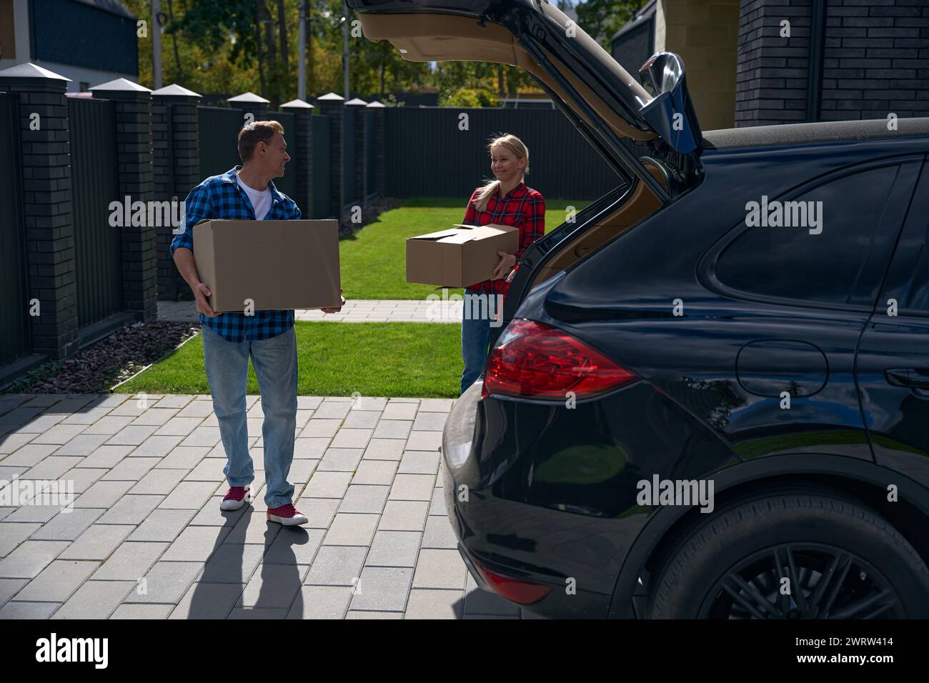 Joyful couple holding cardboard boxes in hands while going to load them ...