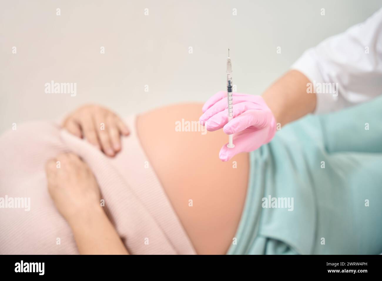 Person in white robe and safety gloves holding syringe with liquid ...