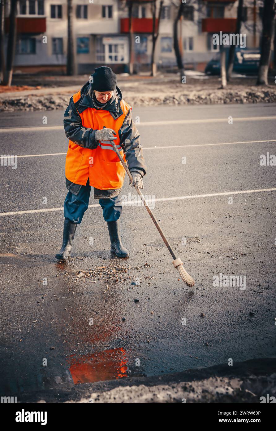 old janitor woman sweeps the street from garbage after winter Stock ...