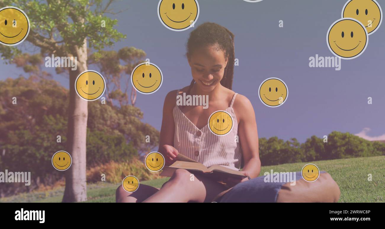 Image of emoji icons over smiling biracial woman reading in park Stock ...