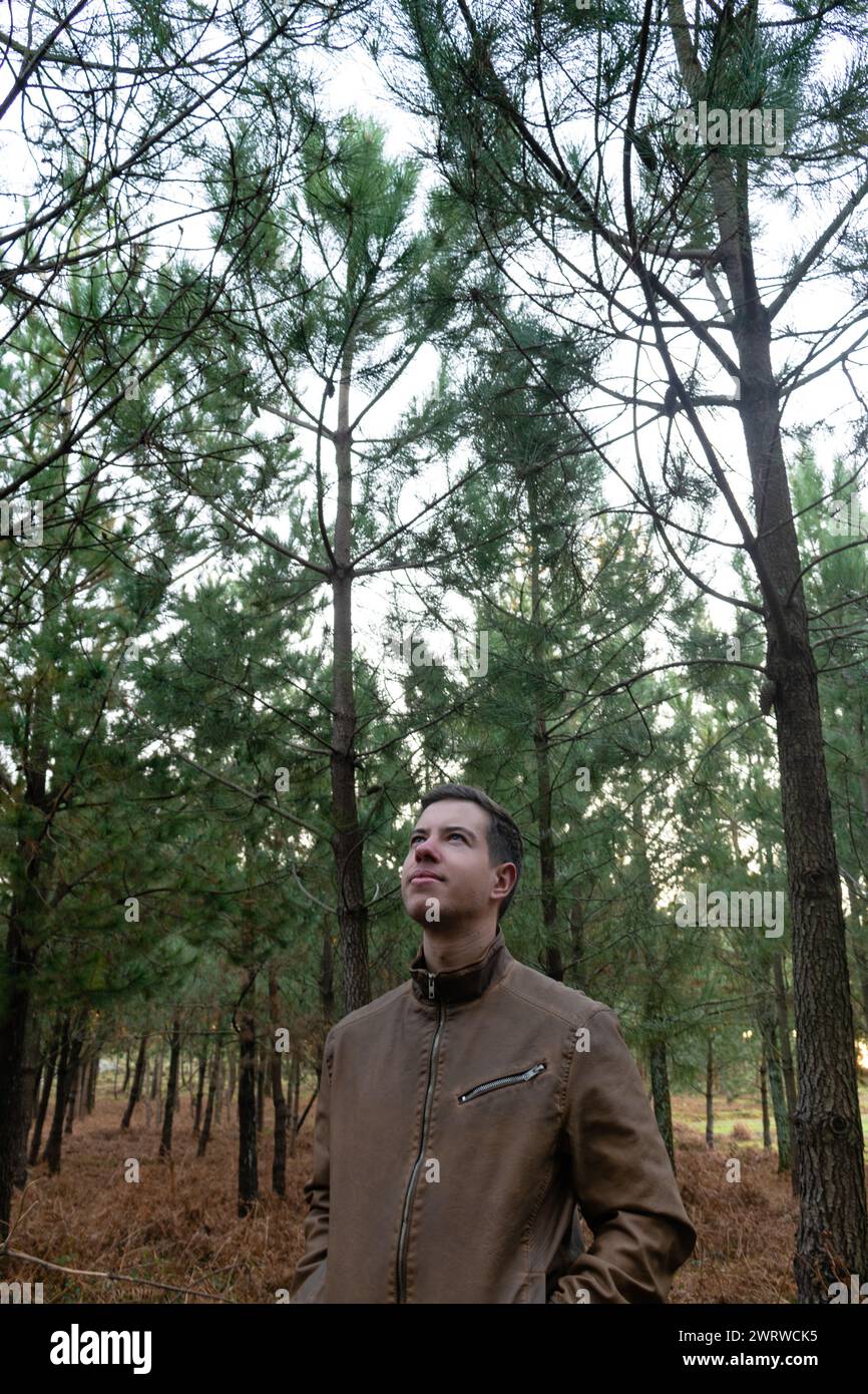 Stock photo of A young man standing alone in a forest looking at the ...