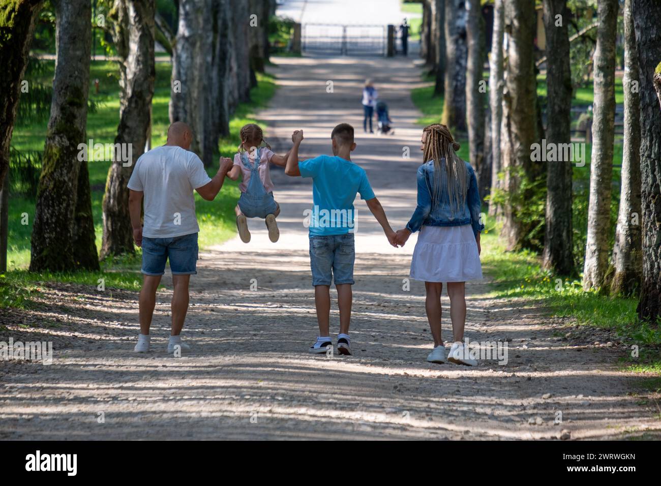 A father playfully swings a child between him and her siblings, as they ...